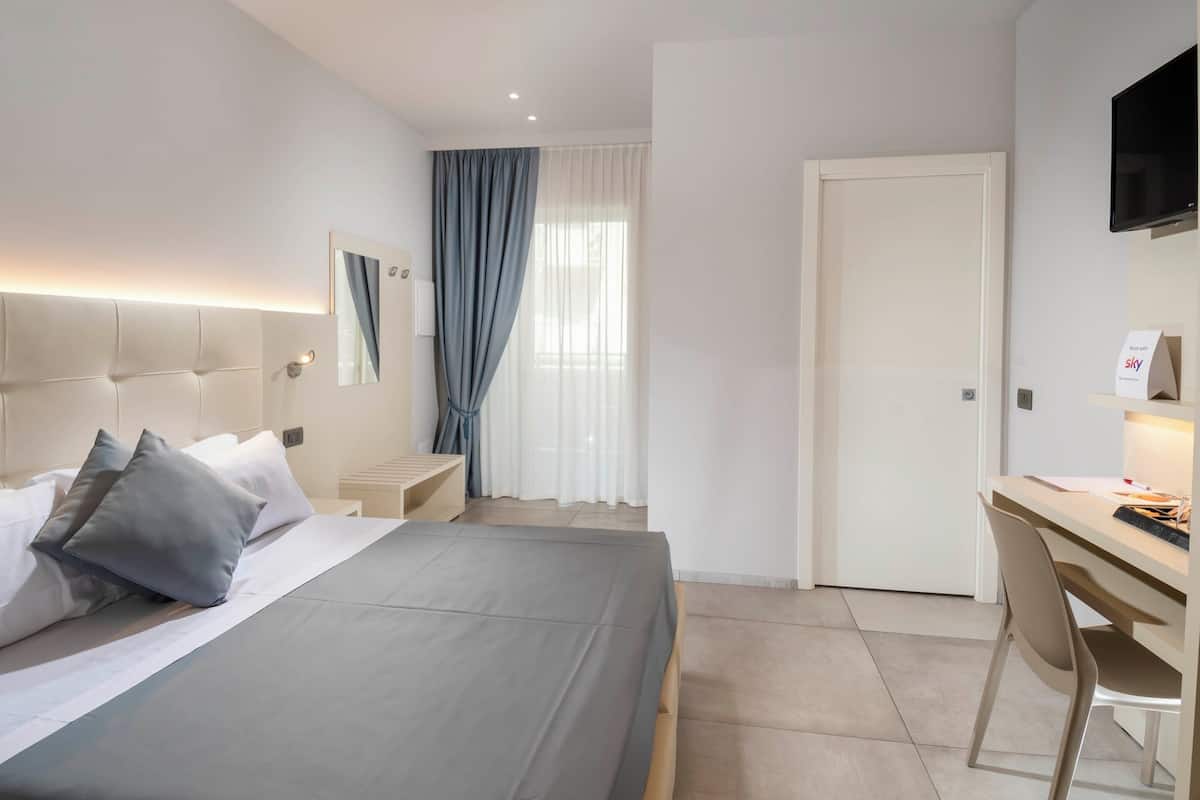 Quarto de hotel moderno com uma cama grande, uma escrivaninha e uma televisão.