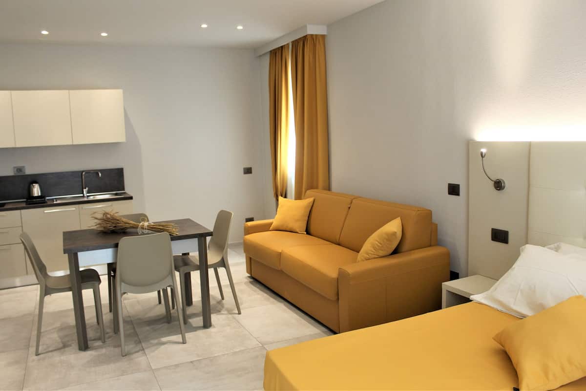 Quarto de hotel moderno com área de refeições, sofá, cama e mesa de cabeceira.