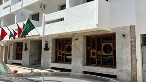 Um edifício com vários andares, paredes externas brancas e varandas. Várias bandeiras estão expostas, incluindo uma verde com um emblema branco.