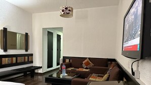 Quarto de hotel com cama, sofá, mesa de centro, televisão e um banco.