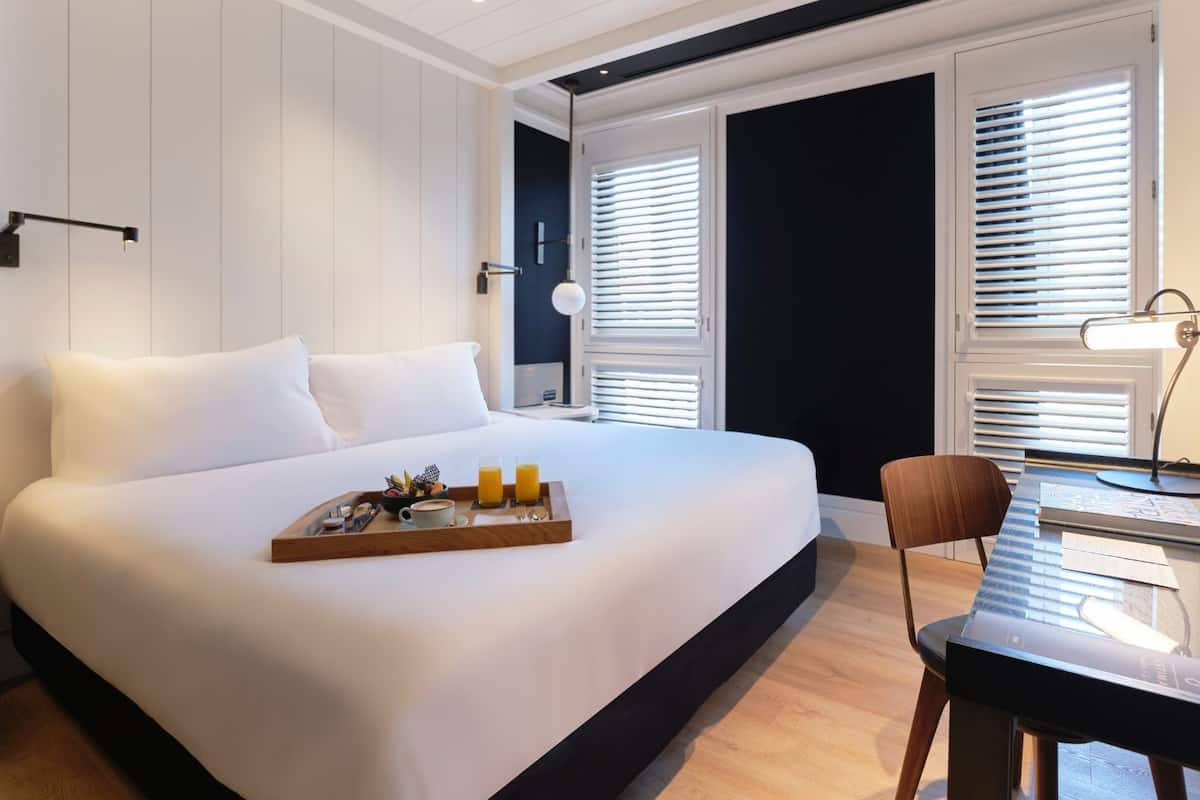 Quarto de hotel moderno com uma cama grande, uma escrivaninha com cadeira e uma bandeja com itens de café da manhã.