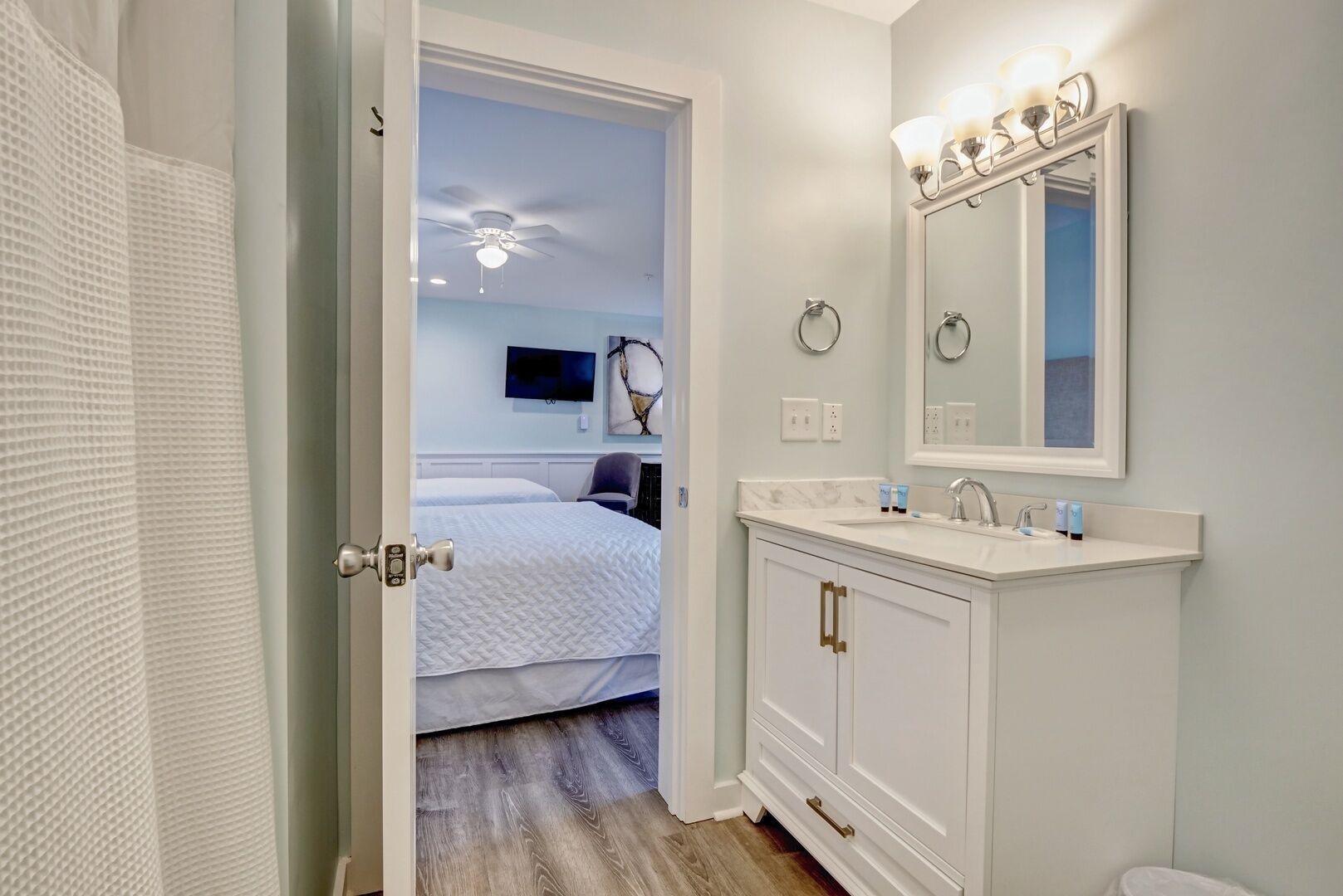 Casa de banho de hotel com toucador branco, espelho grande e ventoinha no teto.