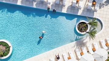 Vista aérea de uma piscina com espreguiçadeiras e guarda-sóis, cercada por um deck revestido.