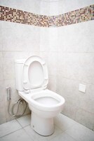 Sanitário branco com tampa, mangueira de chuveiro e parede revestida com mosaico.