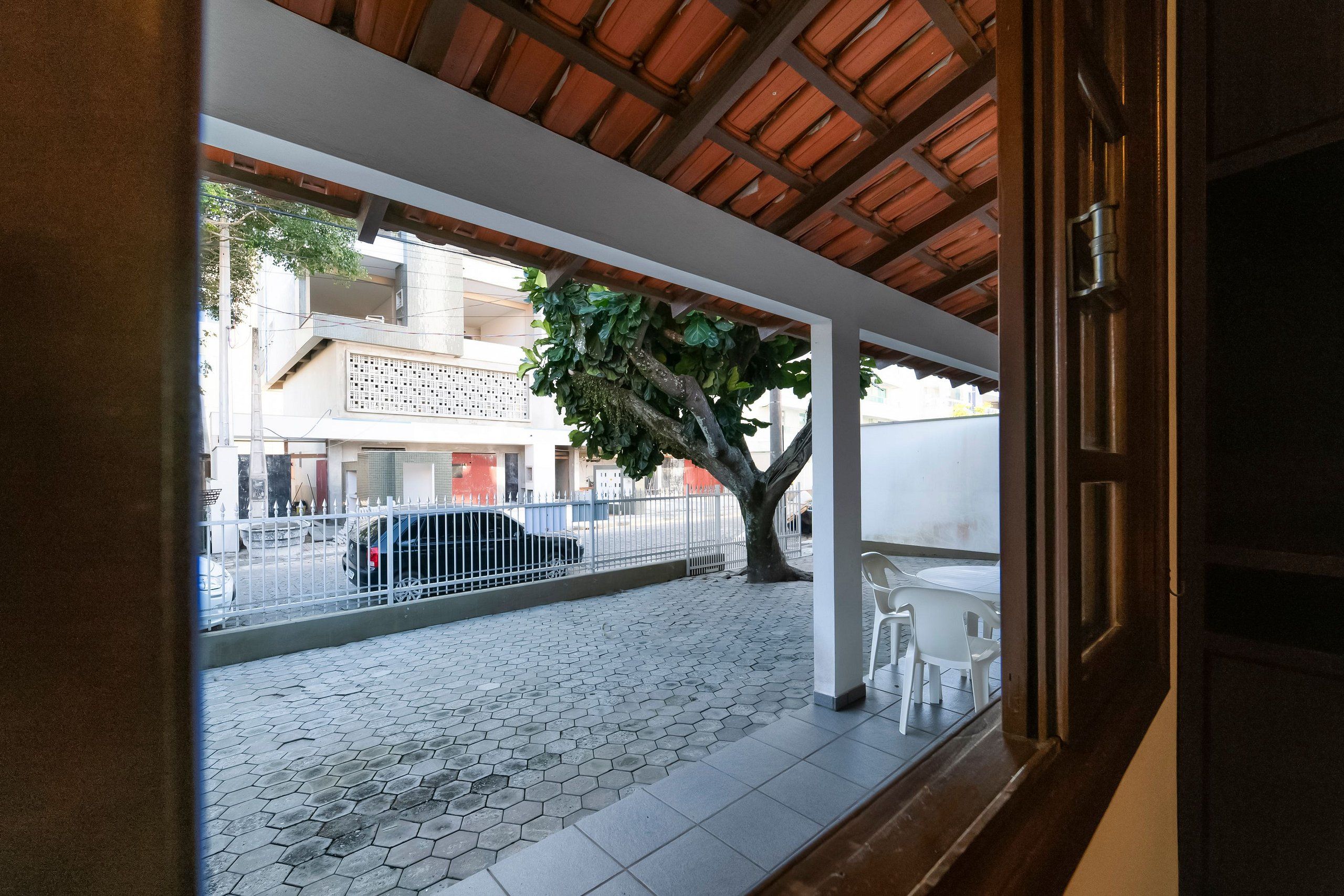 Um espaço ao ar livre coberto com piso de azulejos, uma árvore e um cercado branco.