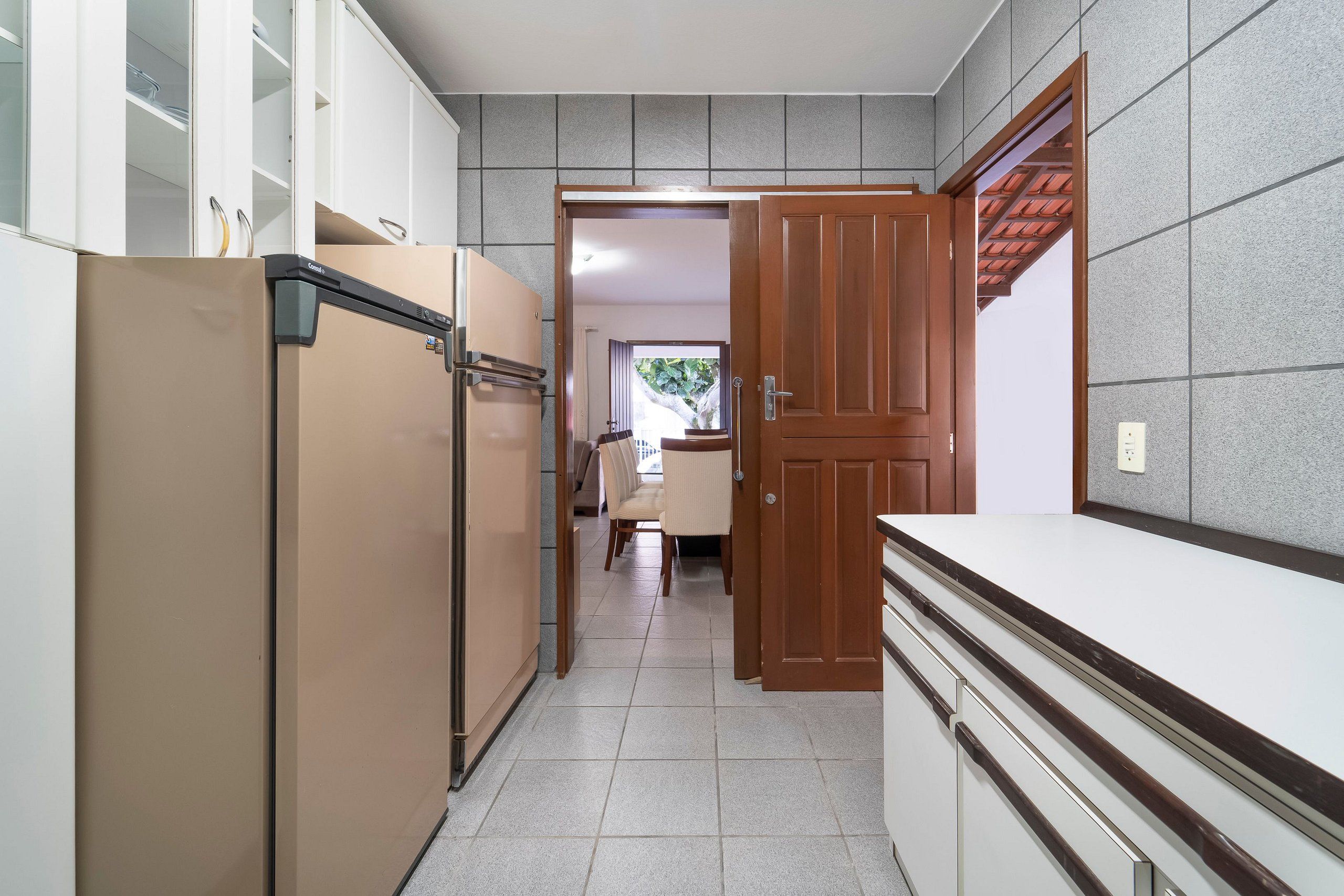 Uma cozinha com geladeira, armários e uma porta de madeira que dá para uma área de refeições.