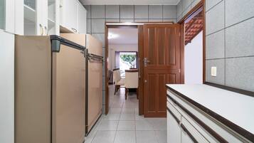 Uma cozinha com geladeira, armários e uma porta de madeira que dá para uma área de refeições.
