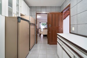 Uma cozinha com geladeira, armários e uma porta de madeira que dá para uma área de refeições.