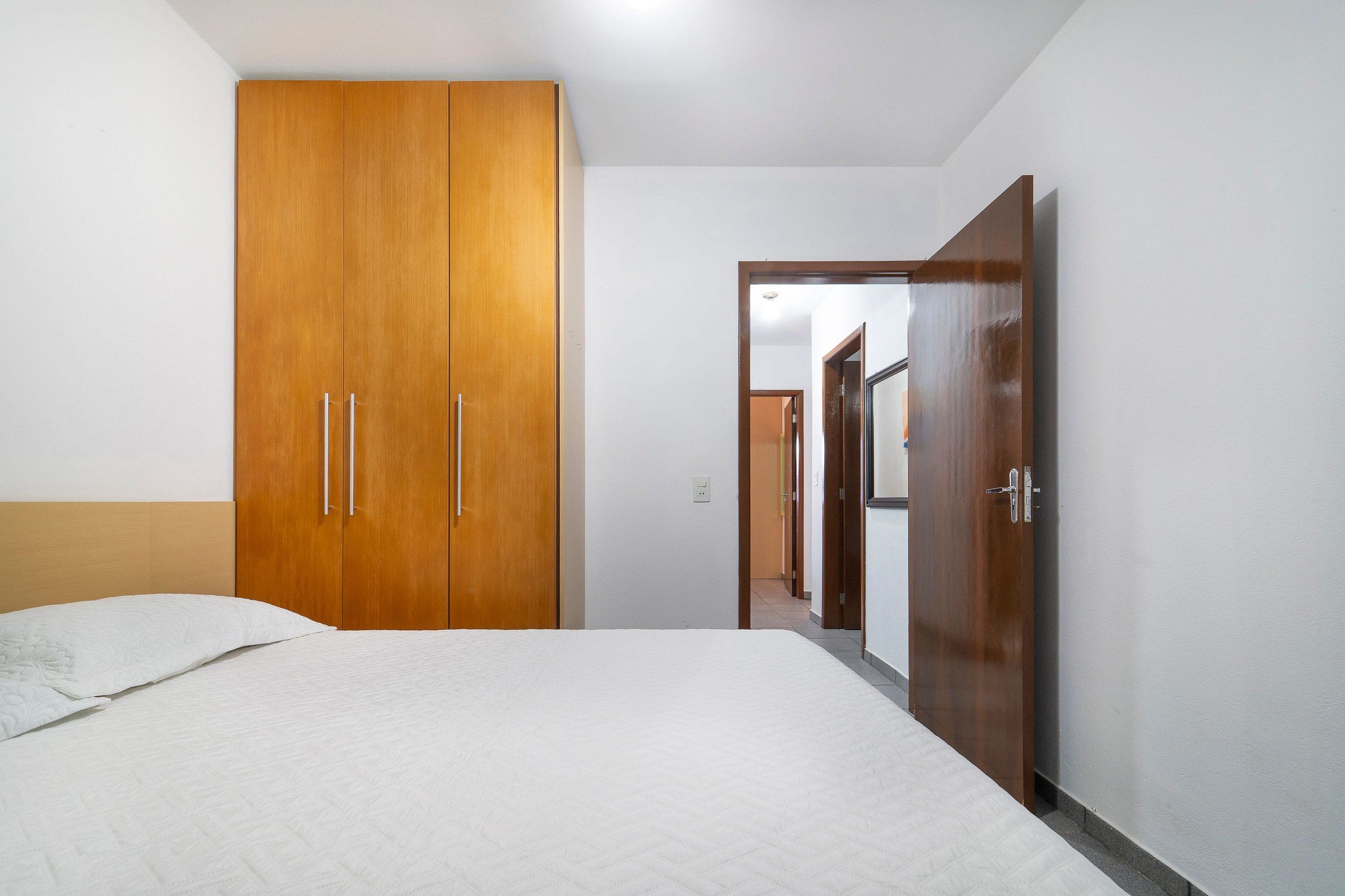 Quarto com cama, guarda-roupa e porta que dá para outro cômodo.