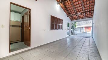 Corredor com piso de azulejos, porta de madeira, janela com persianas e vista para um edifício.