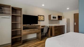 Quarto de hotel com cama, escrivaninha e cadeira, televisão, micro-ondas, frigorífico e guarda-roupa.