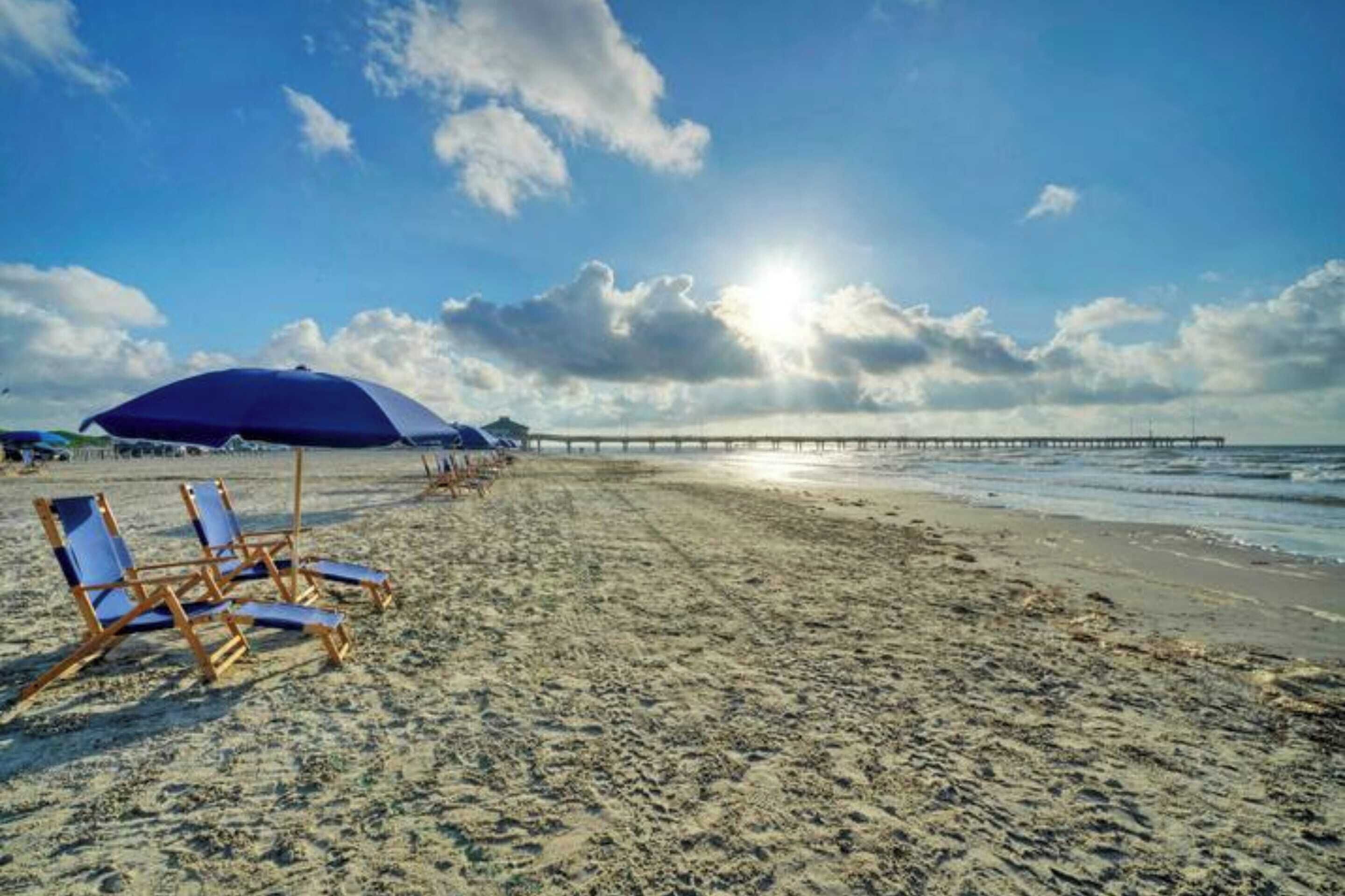 Uma praia com cadeiras de praia azuis e um píer ao fundo.