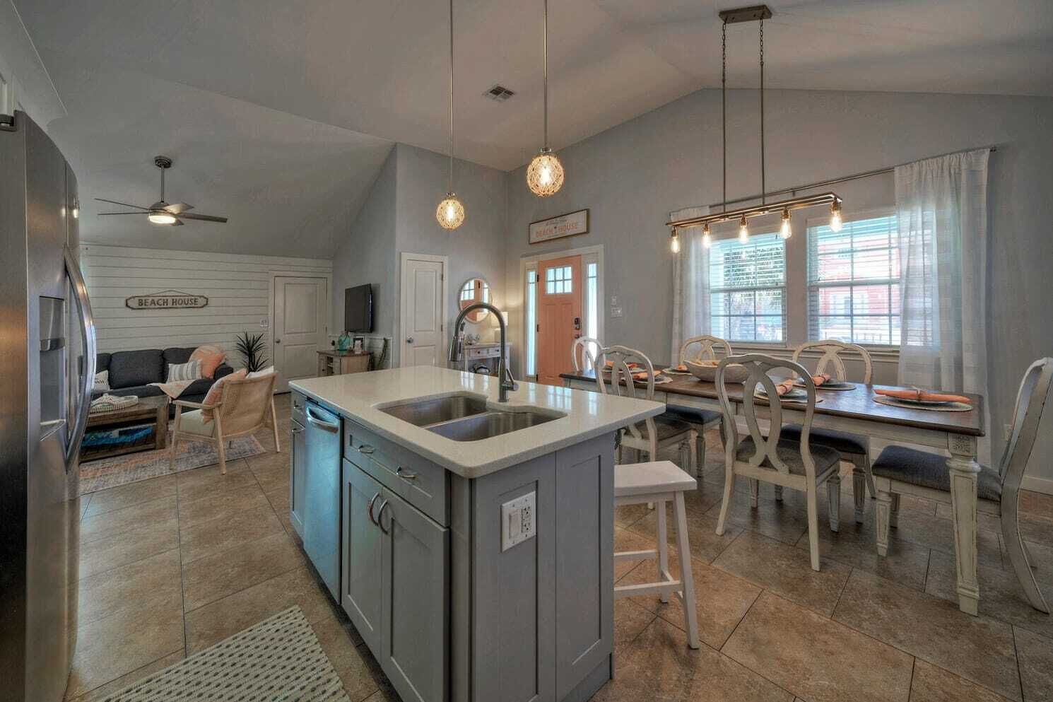 Uma cozinha espaçosa com ilha central, área de jantar com cadeiras brancas e ventilador de teto.
