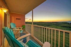 Varanda com duas cadeiras e uma mesa, com vista para uma paisagem gramada ao pôr do sol.