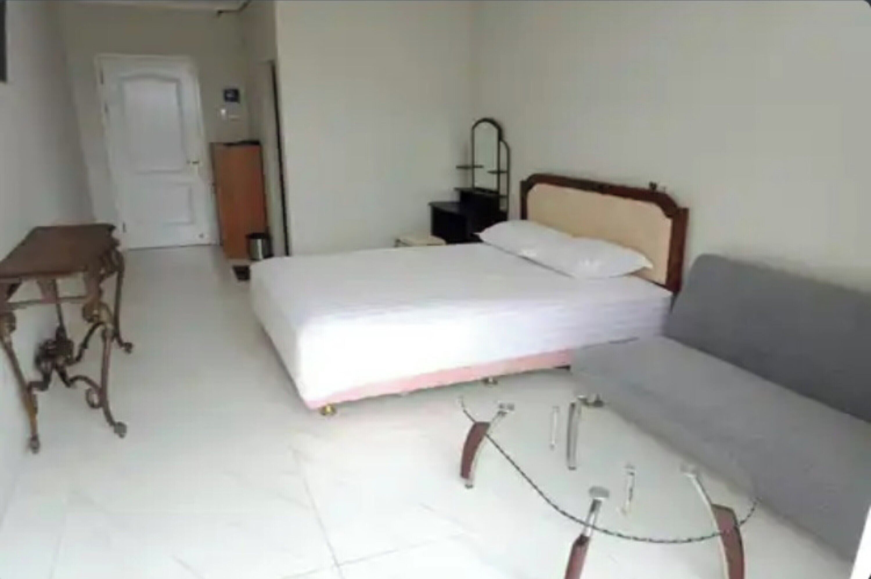 Quarto com cama, mesa de cabeceira, cômoda e sofá cinza.