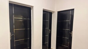 Um corredor com três portas pretas, cada uma com moldura branca e puxador. O chão é ladrilhado, e há um tapete listrado no centro.