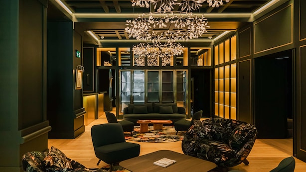 Uma área de estar moderna com piso de madeira, sofás pretos, uma mesa de centro redonda e um candelabro.