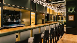 Uma área de bar com um balcão comprido, vários bancos altos e um lustre decorativo no teto.