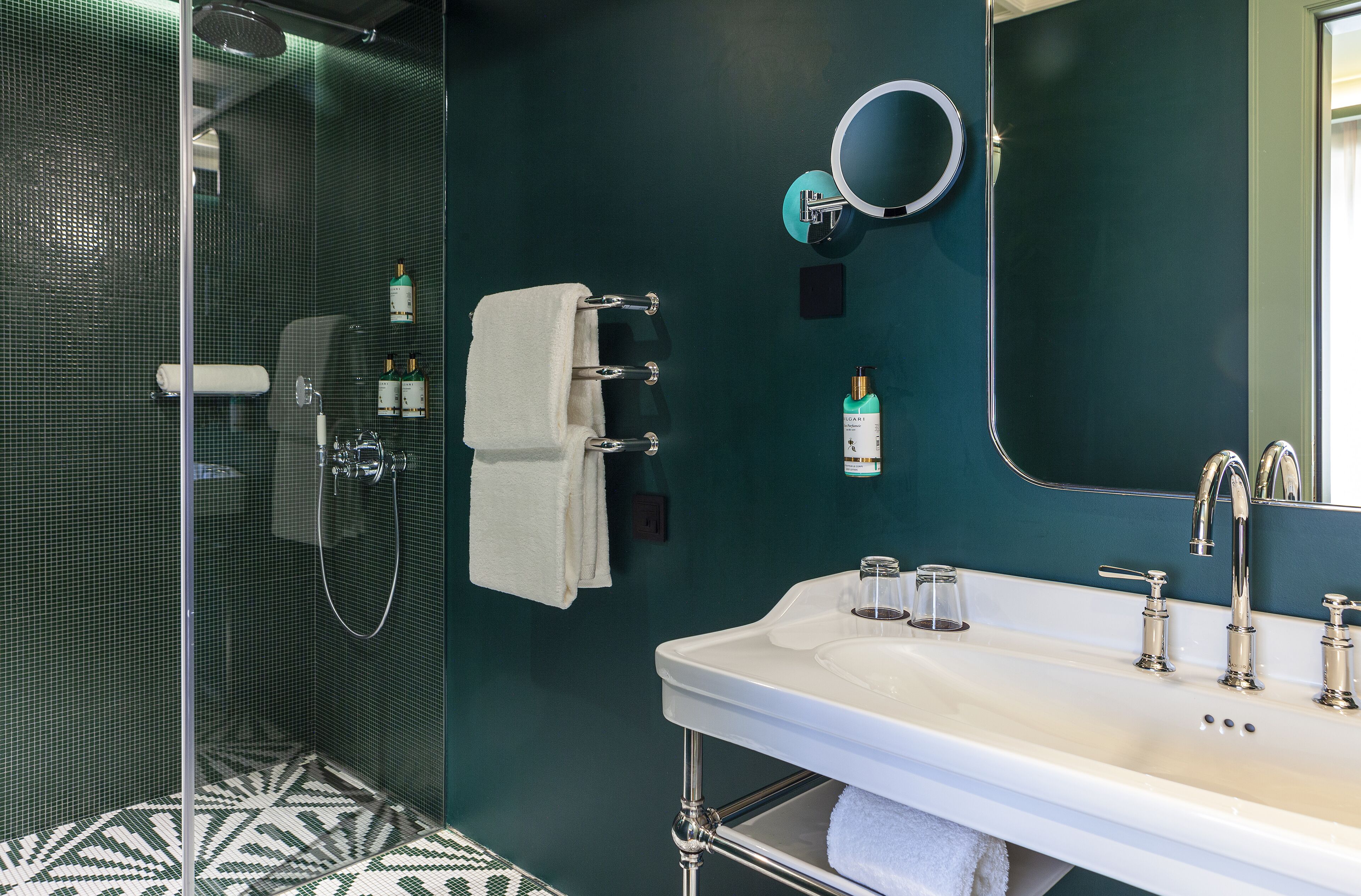 Um banheiro moderno com chuveiro em box de vidro, pia branca com acessórios cromados e parede revestida com azulejos verdes.