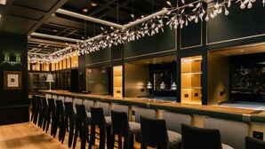 Uma área de bar com um balcão comprido, vários bancos altos e iluminação pendente.