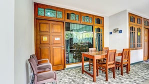 Uma área de refeições com mesa e cadeiras de madeira, chão xadrez e uma grande porta de madeira com painéis de vidro.