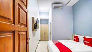 Quarto de hotel com guarda-roupa de madeira, cama com roupa de cama vermelha e branca, televisão na parede e aparelho de ar condicionado.