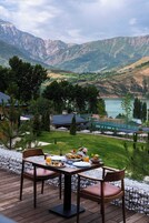 Mesa de jantar com cadeiras em um deck com vista para uma paisagem montanhosa e um lago.