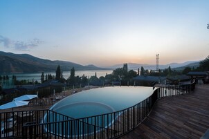 Piscina com deck de madeira e vista para um lago e montanhas.