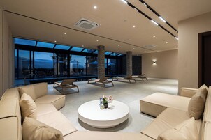 Uma sala de estar ampla com uma mesa de centro redonda, sofás bege e uma grande janela com vista para o exterior.