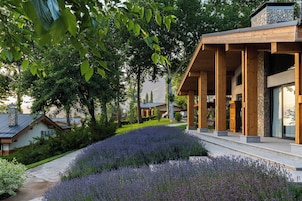 Uma casa moderna com fachada de pedra e vigas de madeira, rodeada por um jardim com lavanda.