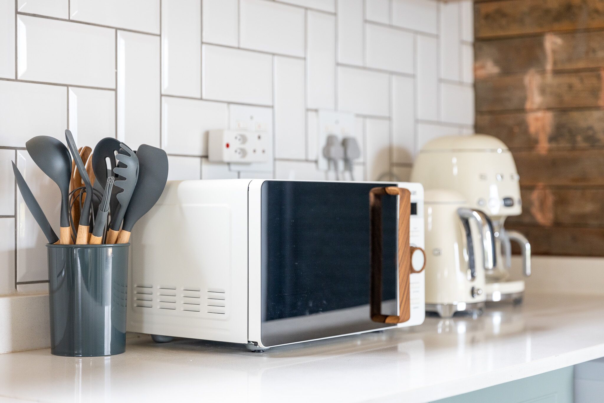 Cozinha com micro-ondas, cafeteira e utensílios em suporte.