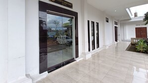 Entrada de um hotel moderno com porta de vidro, uma placa acima da porta e piso ladrilhado.