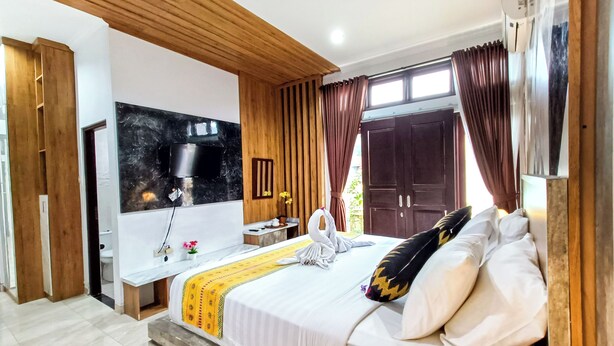 Quarto de hotel com cama, escrivaninha, televisão e janela com cortinas.