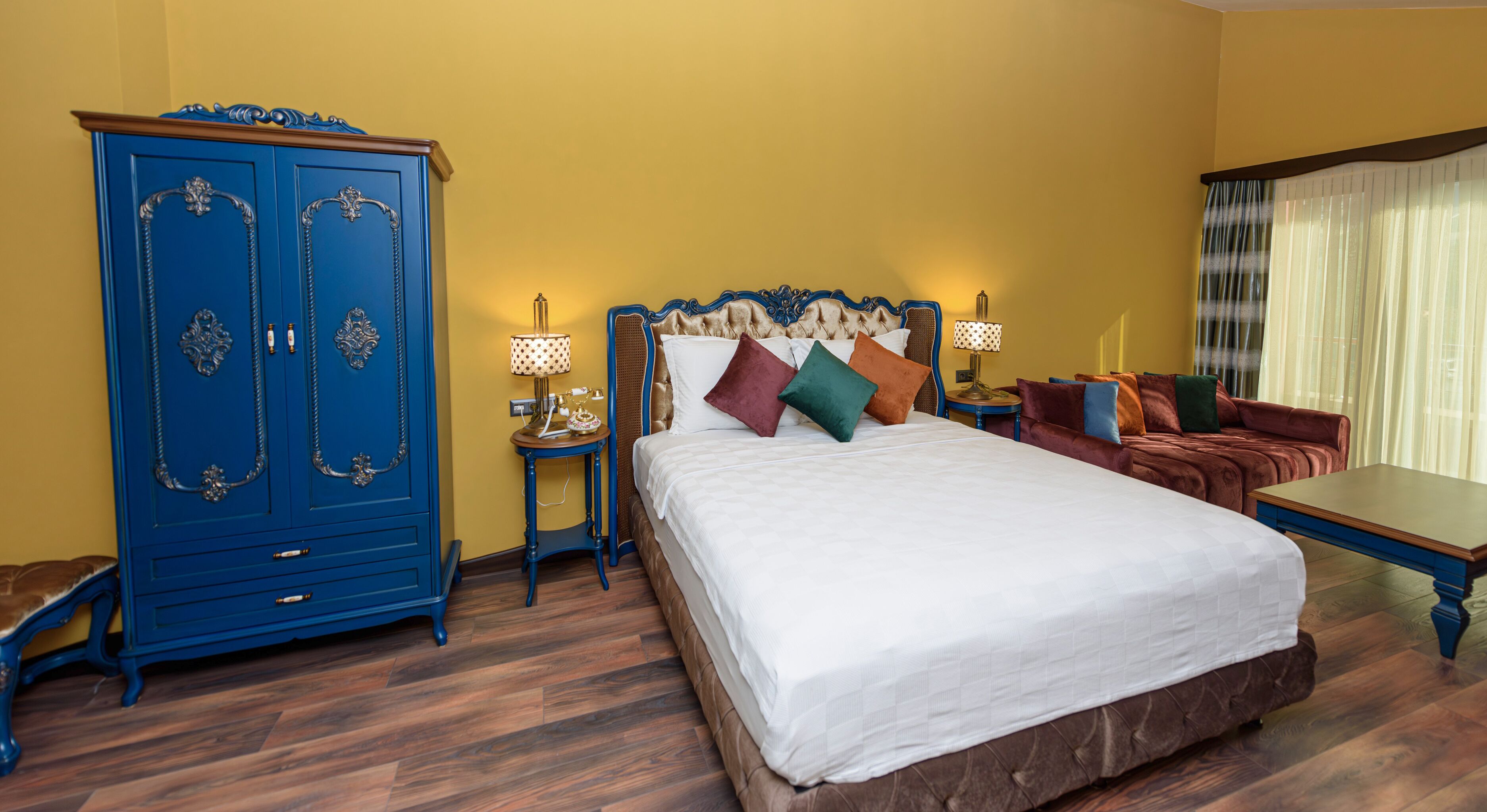Quarto de hotel com uma cama grande, um guarda-roupa, um sofá e duas luminárias.
