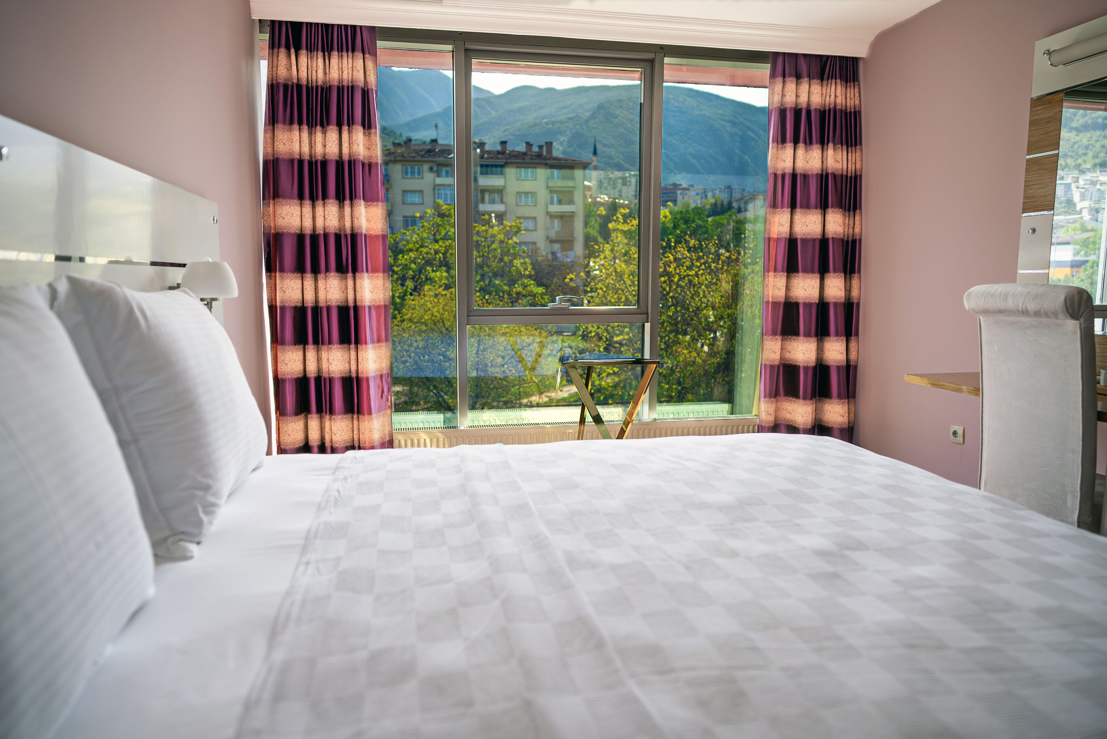 Quarto de hotel com uma cama grande, uma mesa pequena e vista para as montanhas pela janela.