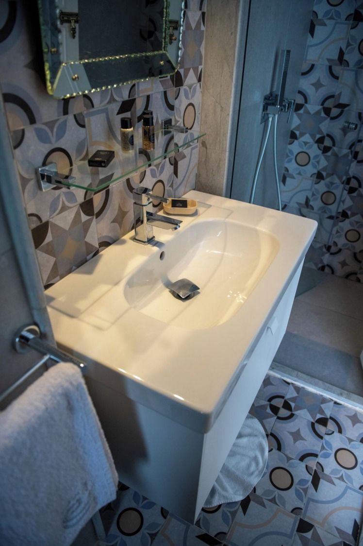 Casa de banho com lavatório branco, prateleira de vidro com artigos de higiene e azulejos estampados.