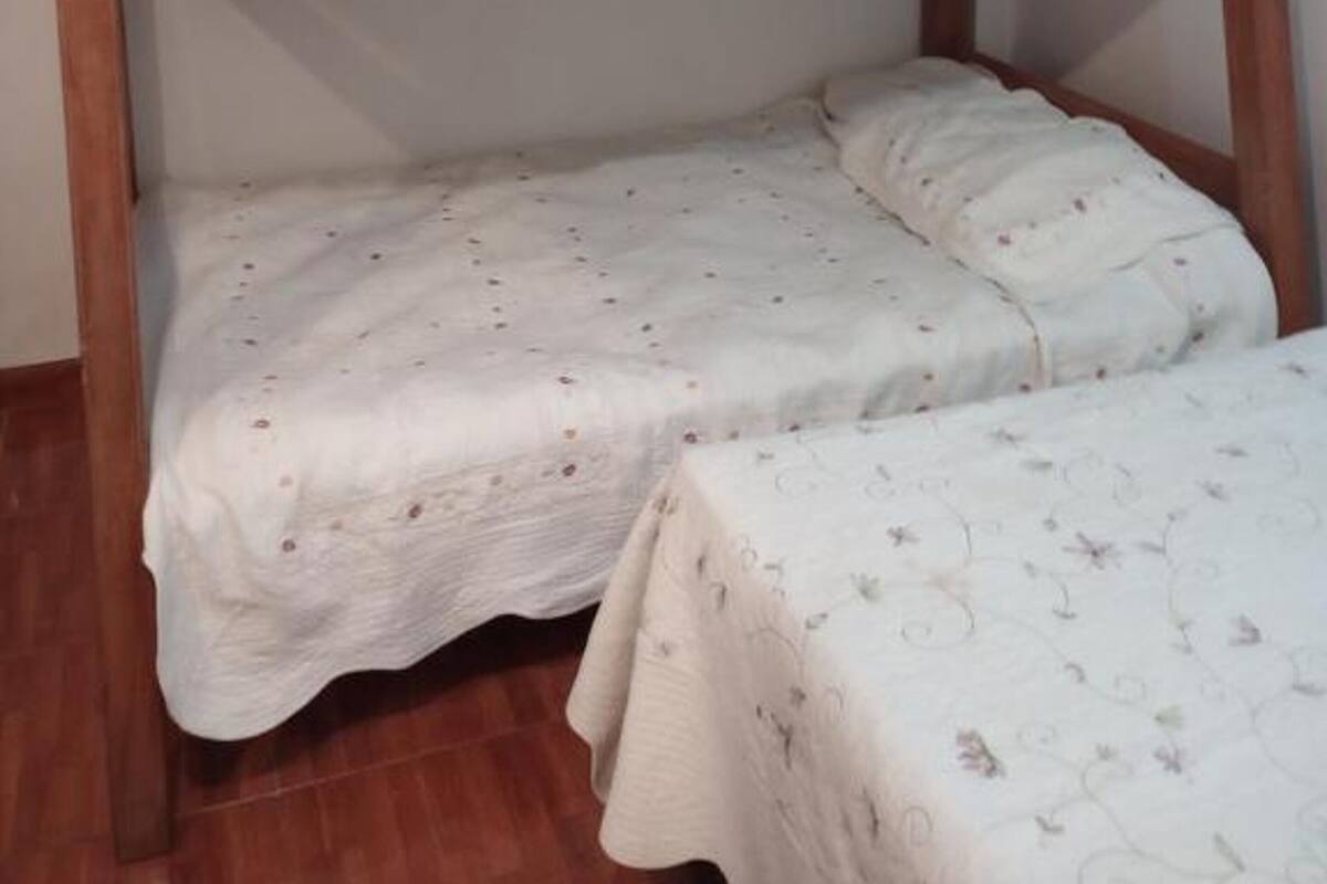 Uma cama beliche com beliche superior azul e duas camas brancas com estampas florais.