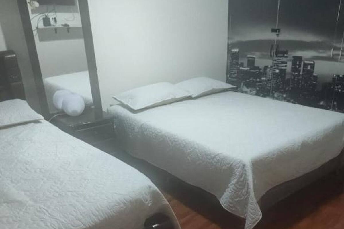Quarto com duas camas de solteiro, cabeceira de madeira, espelho e vista para a cidade pela janela.