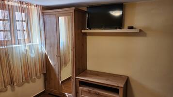 Quarto com guarda-roupa, televisão presa à parede e uma pequena mesa de cabeceira de madeira.