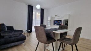 Uma sala de estar moderna com sofá, cadeiras, mesa de jantar e televisão na parede.