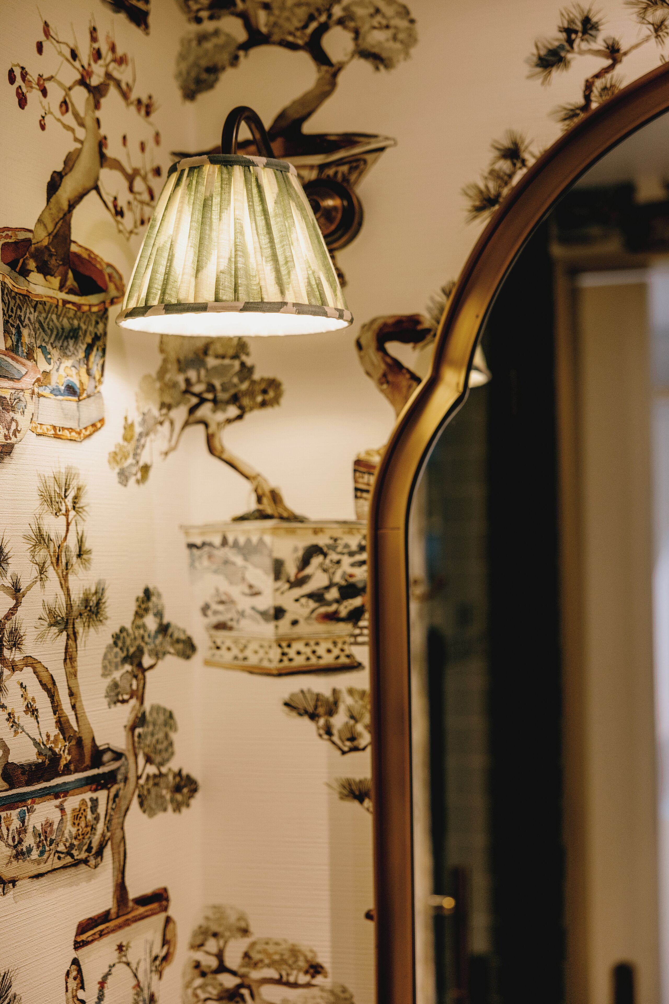 Um quarto com abajur tradicional, espelho e detalhes decorativos na parede.