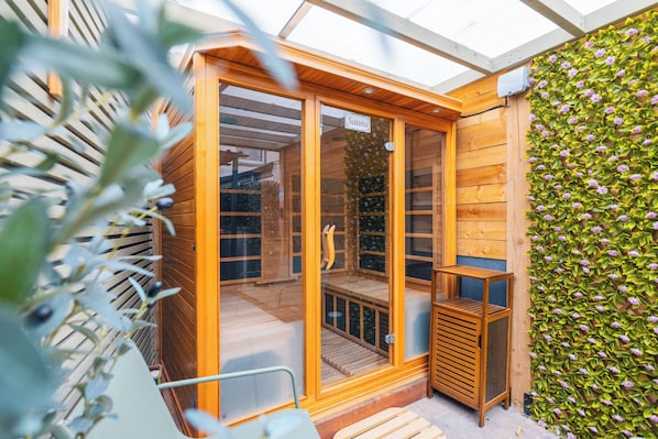 Uma sauna com paredes de madeira e porta de vidro, um banco de madeira e uma pequena mesa.