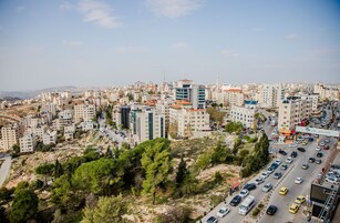 Paisagem urbana com edifícios residenciais densos, um moderno arranha-céu em destaque e uma rua movimentada com carros.