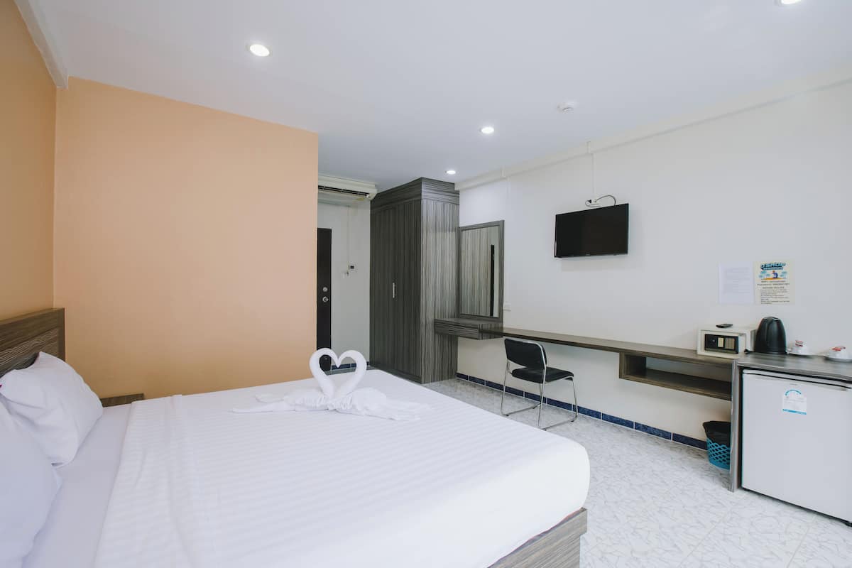 Quarto de hotel com cama bem arrumada, escrivaninha com cadeira, televisão e um pequeno frigorífico.