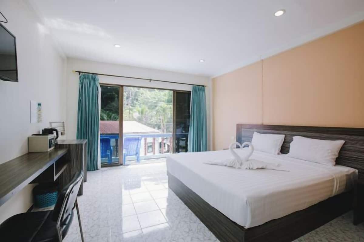 Quarto de hotel com cama, escrivaninha, televisão e varanda com cortinas.
