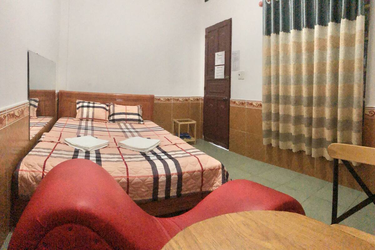Quarto com cama, uma mesinha, uma cadeira e uma porta.