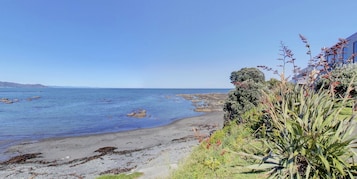 Vista costeira com praia de areia, linha costeira rochosa e água azul cristalina.