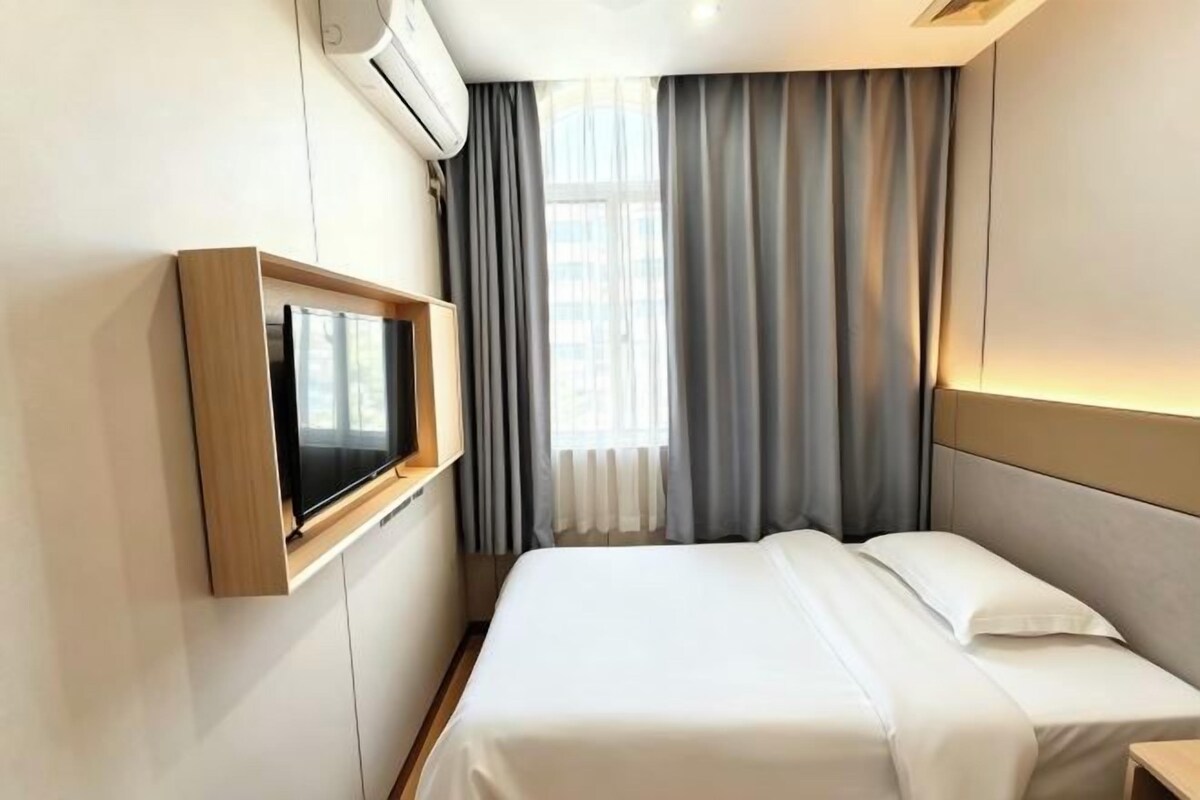 Quarto de hotel com cama, televisão na parede e janela com cortinas.