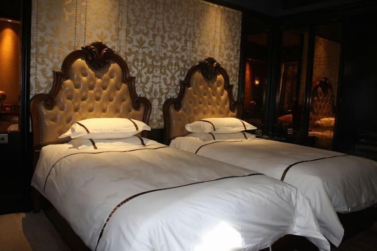 Quarto de hotel com duas camas, cada uma com cabeceira estofada e roupa de cama branca.