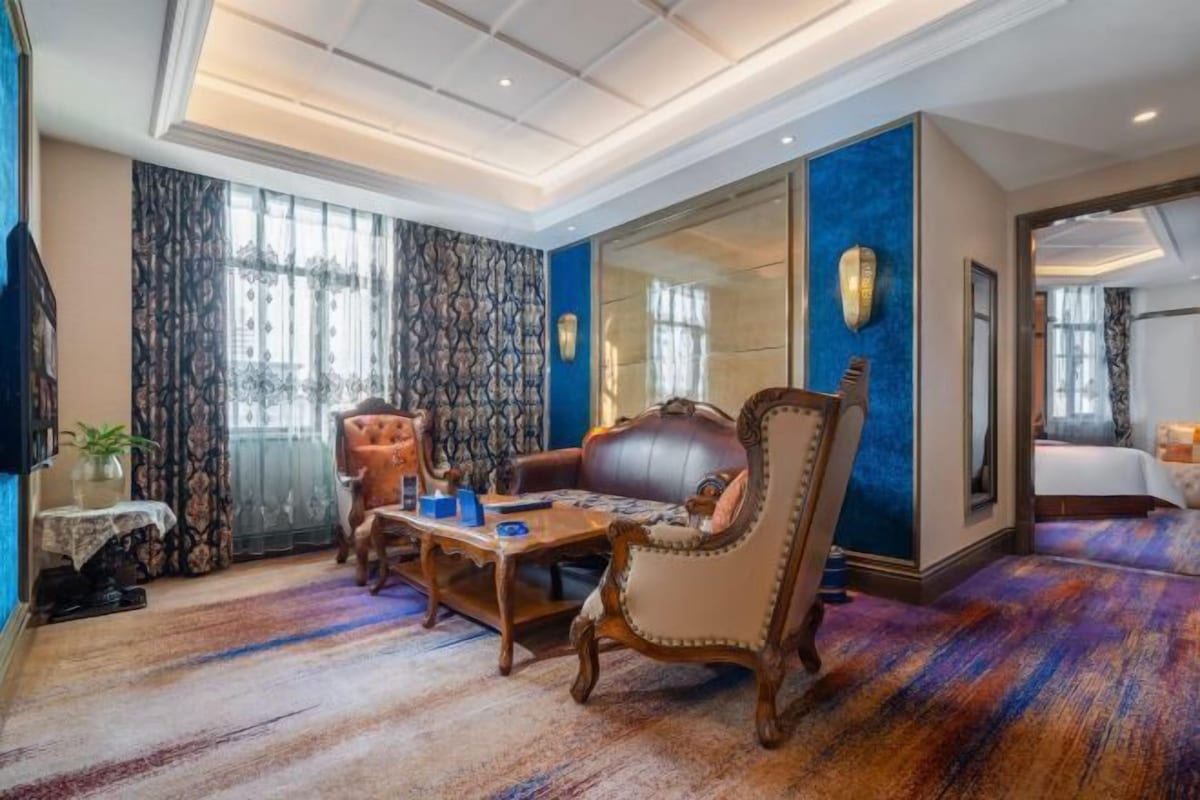 Quarto de hotel com uma cama grande, área de estar com mesa e cadeiras, um espelho grande e vista do interior do quarto.